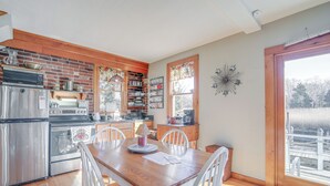 Cozinha com backsplash de tijolos, eletrodomésticos de aço inoxidável e área de refeições com mesa de madeira e cadeiras brancas.