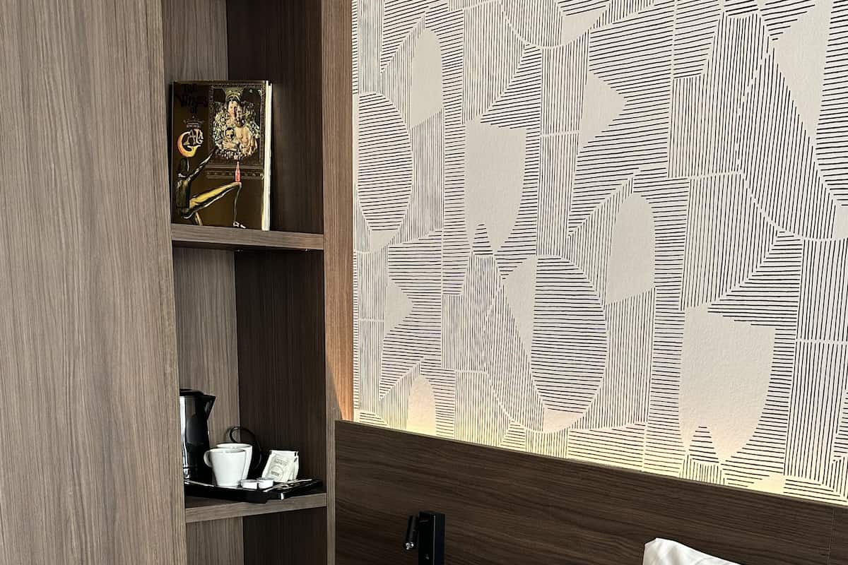 Um quarto com cama, mesa de cabeceira, prateleira com livros, parede decorativa e papel de parede estampado.
