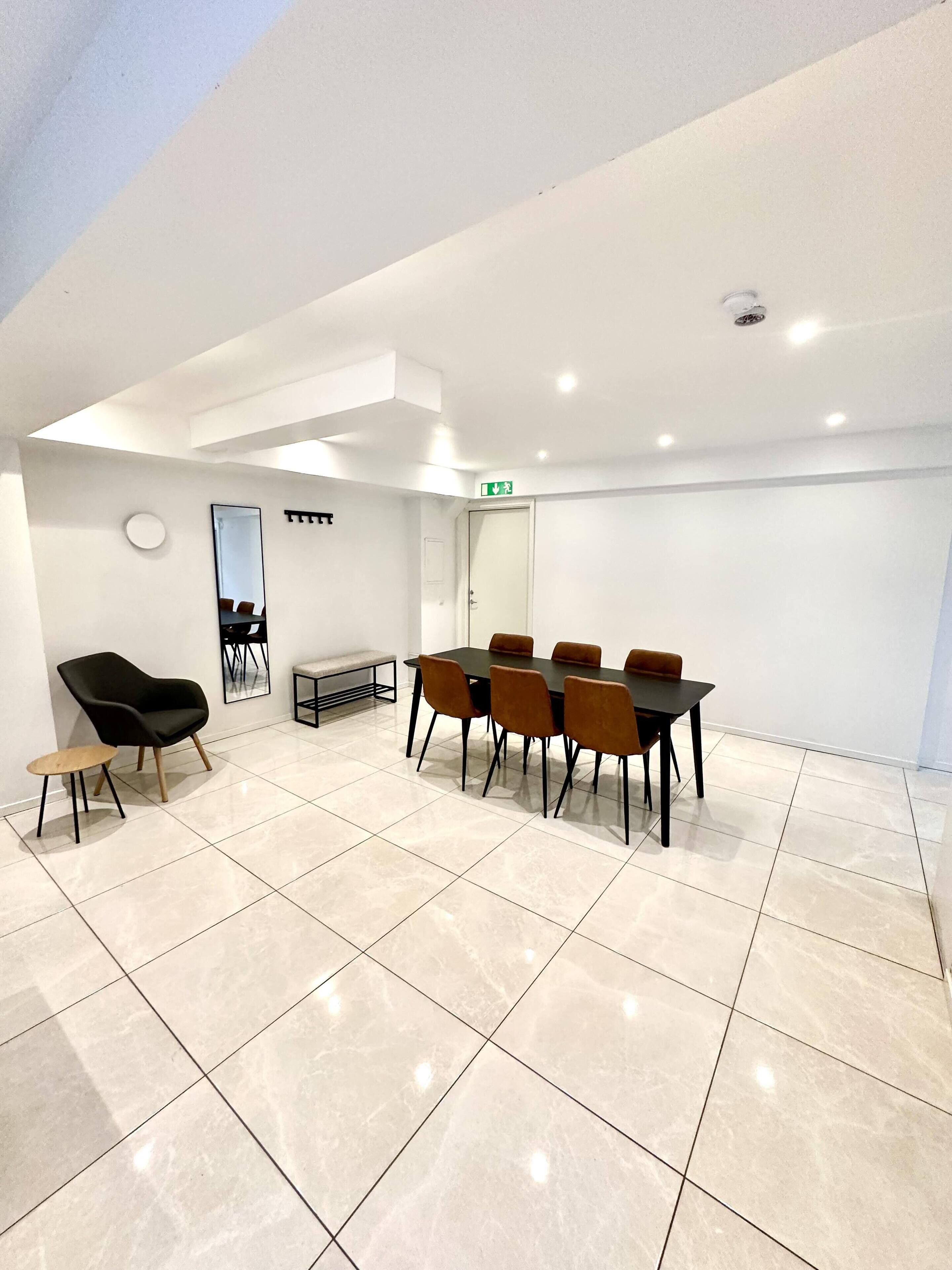 Uma sala de reuniões moderna com uma mesa retangular e seis cadeiras, uma poltrona preta, uma pequena mesa redonda e um banco.