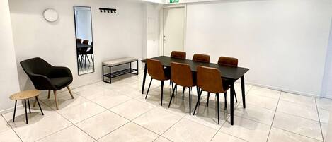 Uma sala de reuniões moderna com uma mesa retangular e seis cadeiras, uma poltrona preta, uma pequena mesa redonda e um banco.