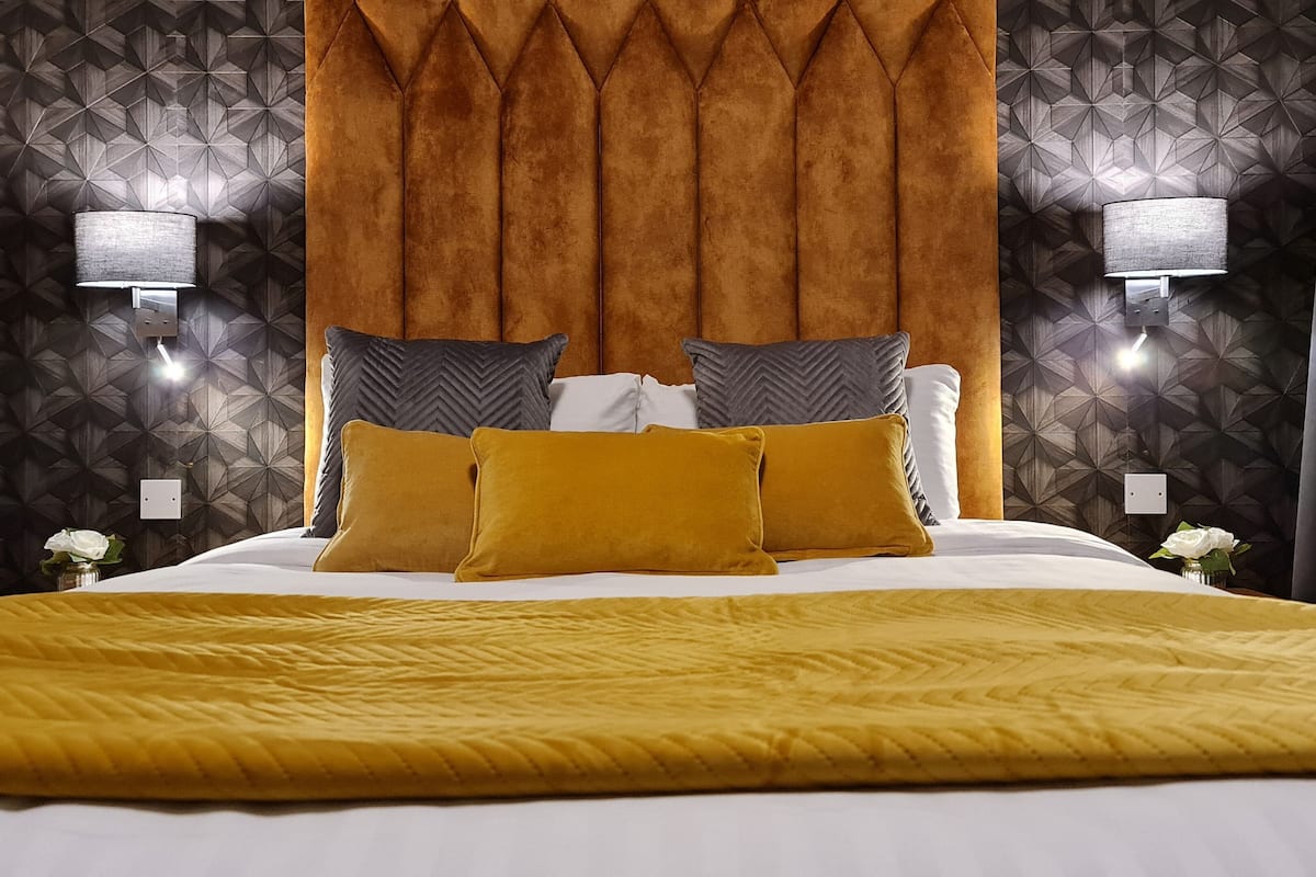 Quarto de hotel com uma cama grande, cabeceira estofada e papel de parede com padrão geométrico.
