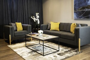 Uma sala de estar moderna com dois sofás cinzas, almofadas amarelas, uma mesa de centro e um vaso com flores brancas.