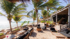 Um lounge à beira-mar com mobiliário de madeira, palmeiras e vista para o oceano.