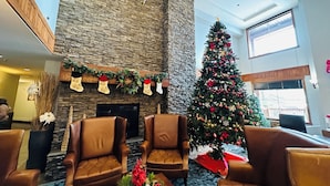 Um hall com poltronas de couro, lareira de pedra, árvore de Natal e uma janela grande.