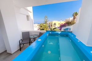 Piscina no terraço com borda azul, uma pequena mesa e uma cadeira, com vista para área residencial com edifícios e árvores.