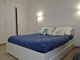 Quarto com cama, guarda-roupa branco e luminária na parede.