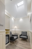 Quarto compacto com claraboia, duas poltronas de couro, uma mesa redonda pequena e um abajur.
