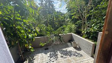 Uma área de pátio com piso de azulejos, rodeada por vegetação densa e árvores.