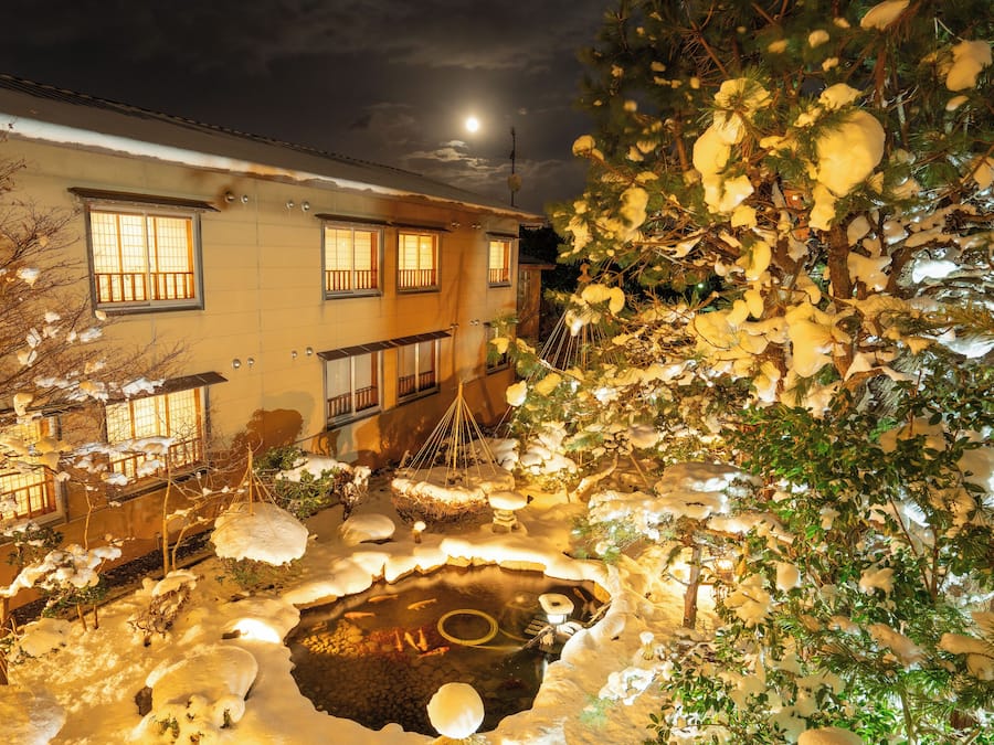Um edifício tradicional japonês com um jardim coberto de neve e um lago.