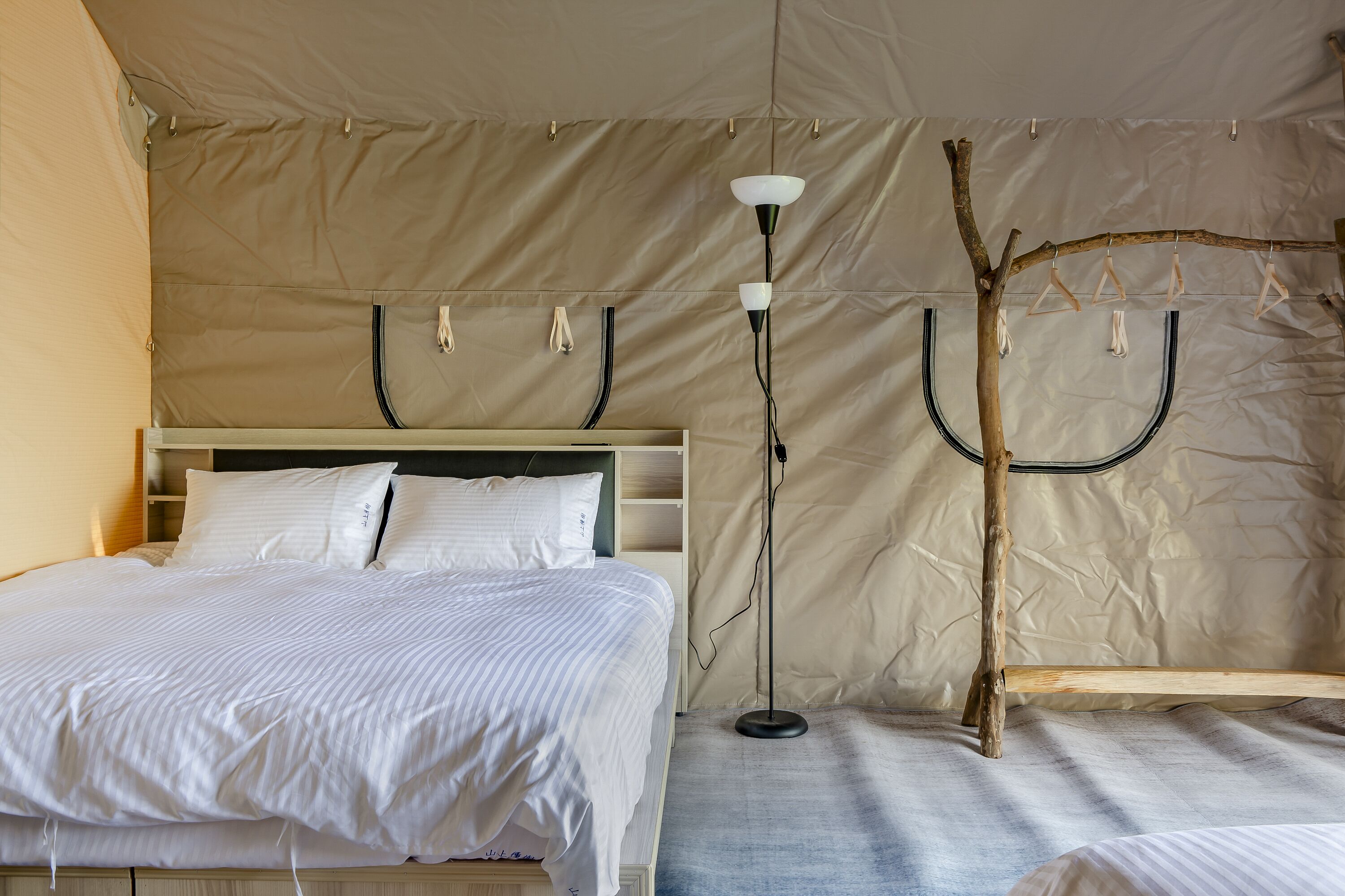 Um quarto com tenda, uma cama, um abajur e um galho de madeira.