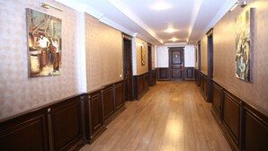 Um corredor com piso de madeira, paredes creme e painéis de madeira escura. Há portas em ambos os lados e obras de arte nas paredes.
