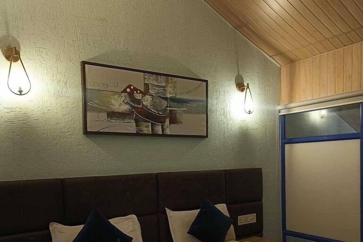Quarto de hotel com uma cama grande, cabeceira com luminária e um quadro pendurado na parede, além de teto de madeira.