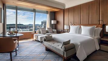 Quarto de hotel moderno com uma cama grande, um sofá, uma escrivaninha e vista para a cidade.