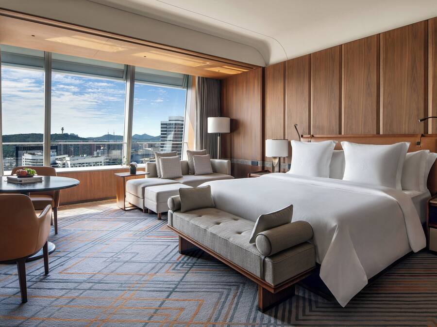 Quarto de hotel moderno com uma cama grande, um sofá, uma escrivaninha e vista para a cidade.