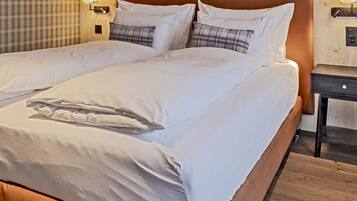 Uma cama bem arrumada com lençóis brancos e almofadas xadrez, uma cabeceira de madeira e uma mesa de cabeceira com um abajur.