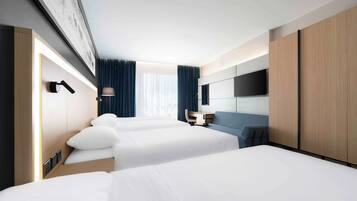 Quarto de hotel com duas camas, uma escrivaninha, uma cadeira, televisão e uma janela grande com cortinas.