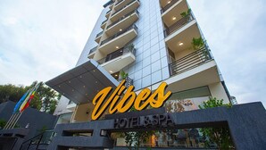 Um hotel moderno com um letreiro chamativo escrito 'Vibes', várias varandas e fachada de vidro.