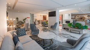 Uma sala de estar ampla, com design moderno, apresentando um sofá grande, poltronas, uma mesa de centro de mármore e uma televisão fixada na parede.