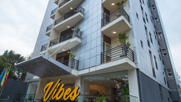 Um hotel moderno com várias varandas, um letreiro chamativo com a palavra 'Vibes' e fachada bem conservada.