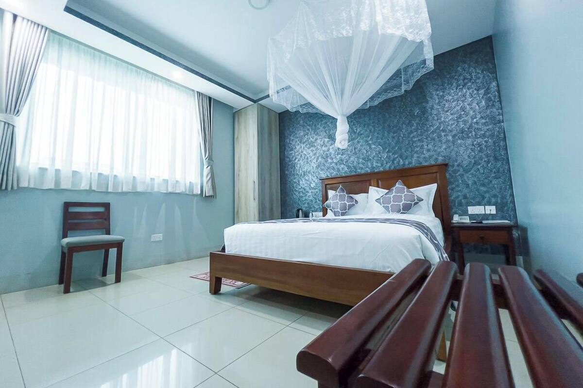 Quarto com cama, cadeira, mesa de cabeceira e um banquinho.