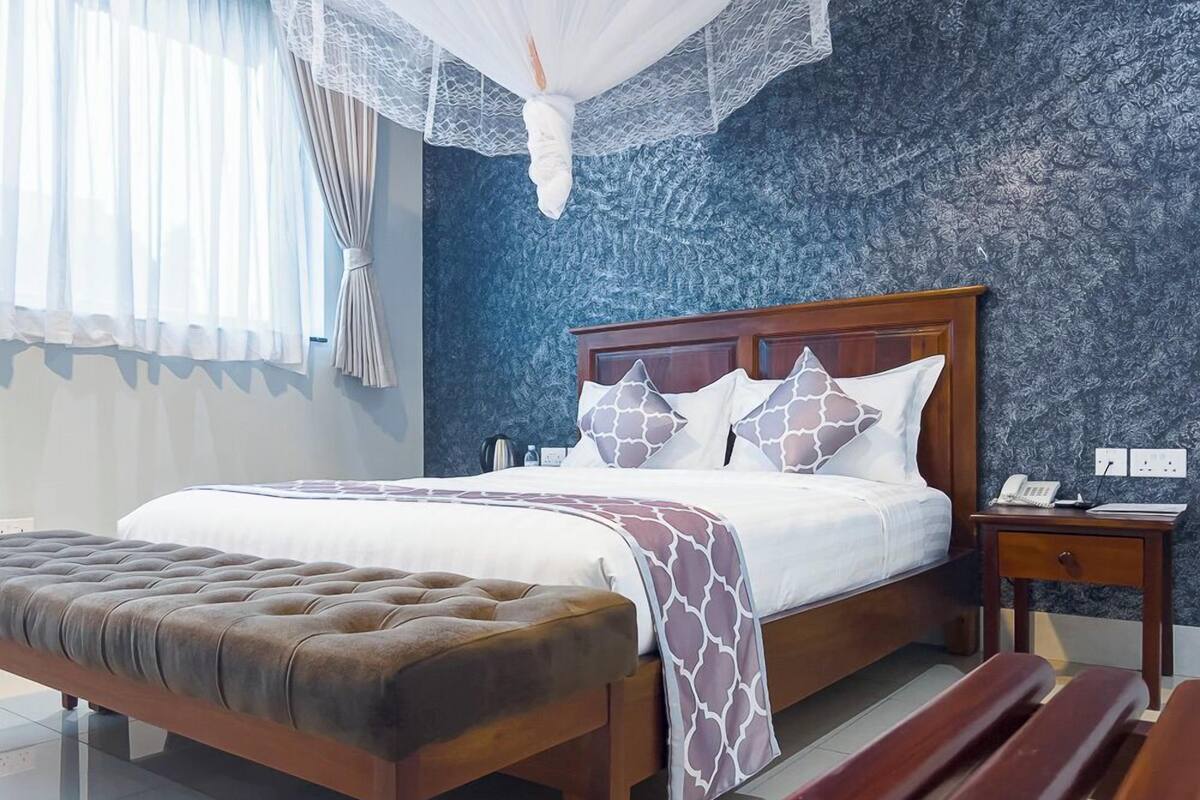 Quarto com cama grande, um banco de madeira, mesa de cabeceira com telefone e parede com textura.