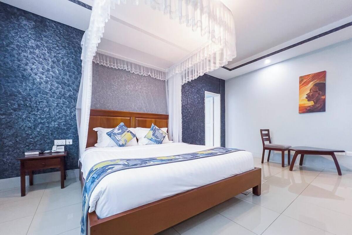 Um quarto com uma cama grande, uma mesinha de cabeceira, uma cadeira e um quadro na parede.