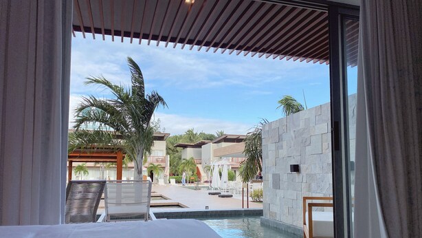 Quarto de hotel com vista para uma piscina, área de estar externa e palmeiras.