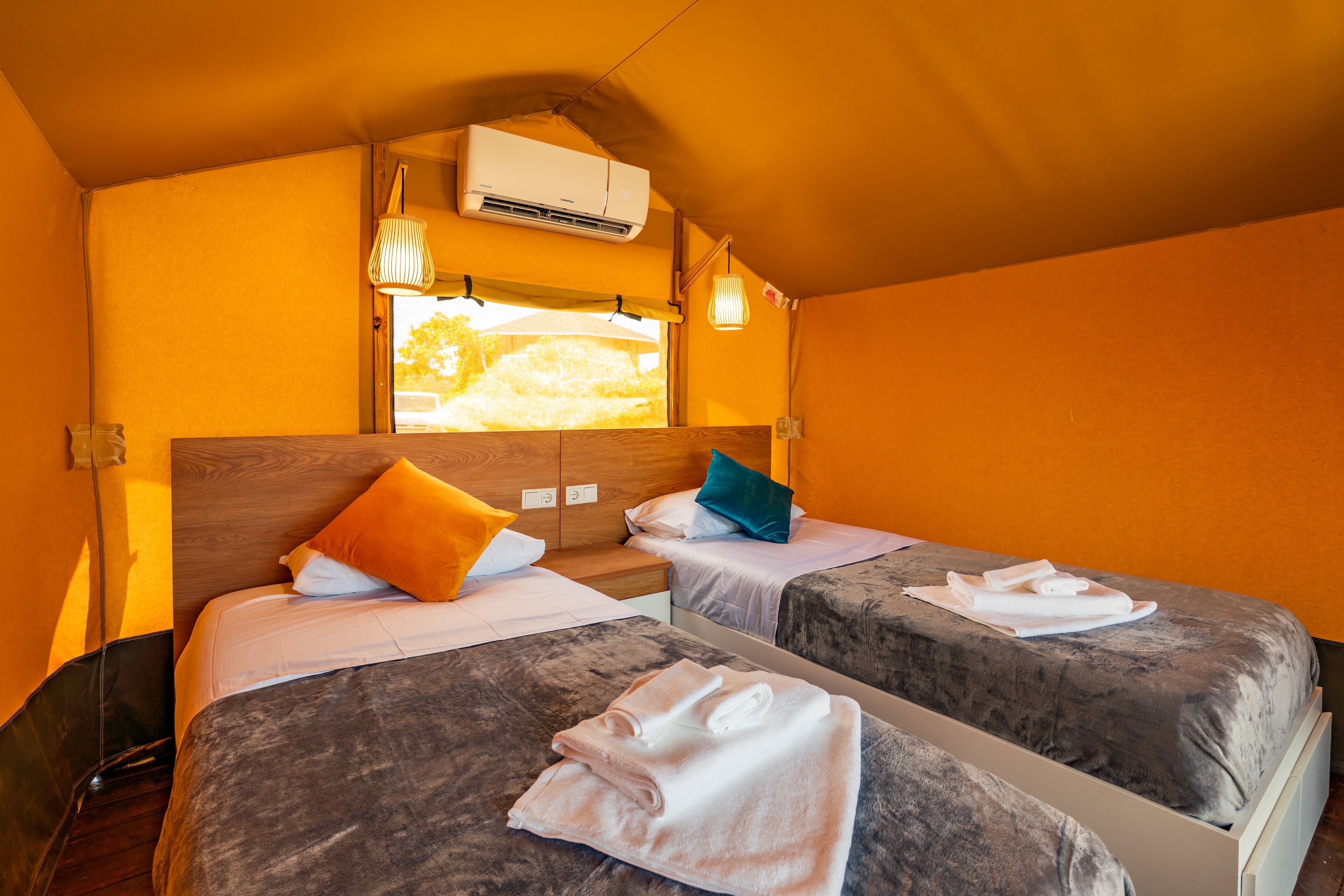 Quarto com duas camas, cada uma com travesseiro e cobertor, e um ar condicionado sobre a janela.