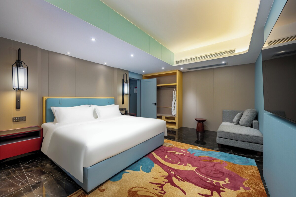 Quarto de hotel moderno com uma cama grande, área de estar e televisão.