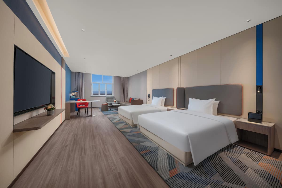 Quarto de hotel moderno com duas camas, televisão, escrivaninha e janela com vista.
