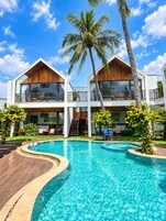 Resort de dois andares com piscina, palmeiras e céu azul límpido.