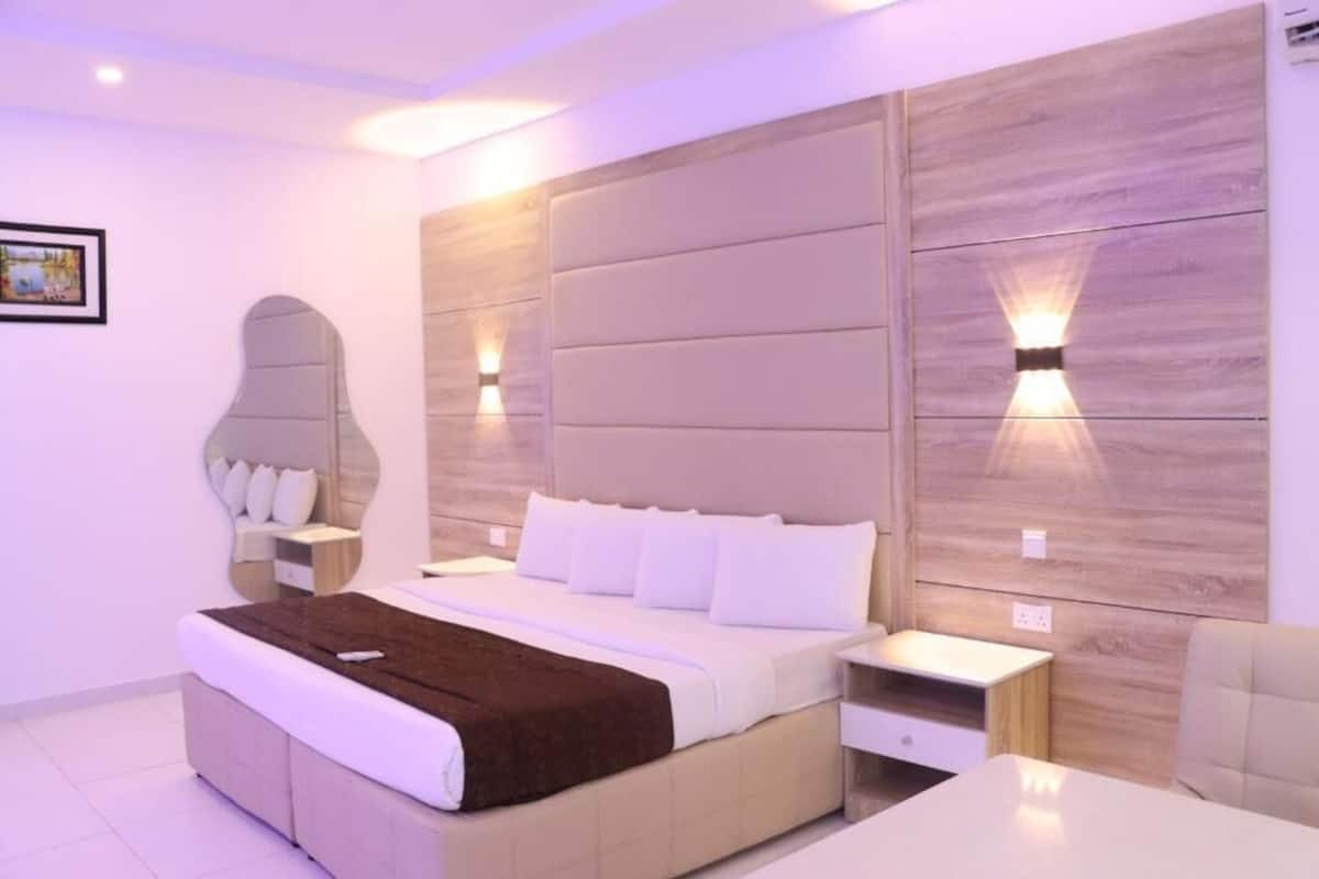 Quarto moderno com uma cama grande, mesas de cabeceira e iluminação embutida na parede.