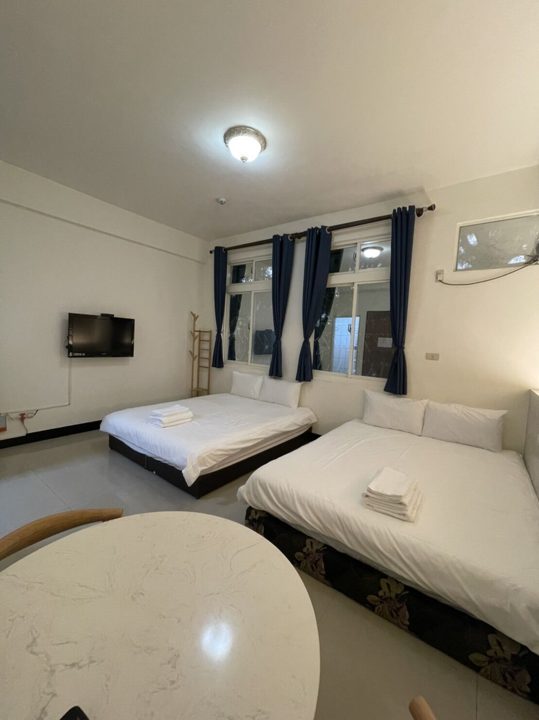Quarto de hotel com duas camas, televisão, mesa pequena e janela com cortinas.