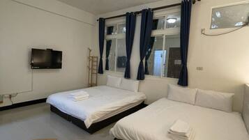 Quarto de hotel com duas camas, televisão, mesa pequena e janela com cortinas.