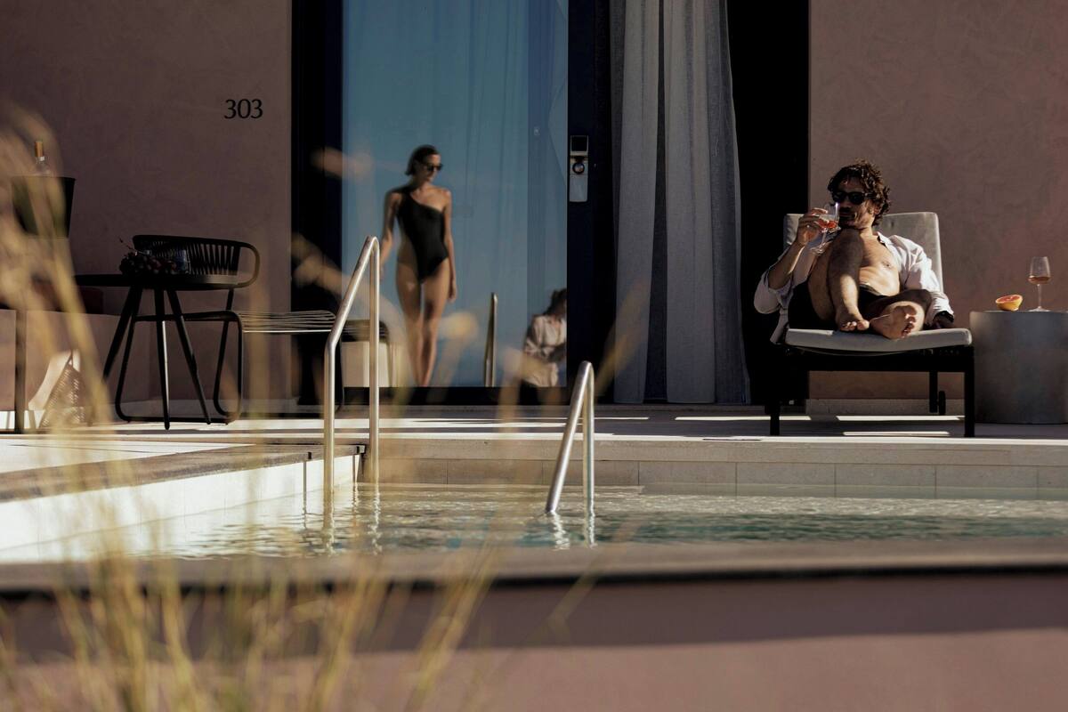Área da piscina com uma cadeira e uma pessoa sentada à beira da água.