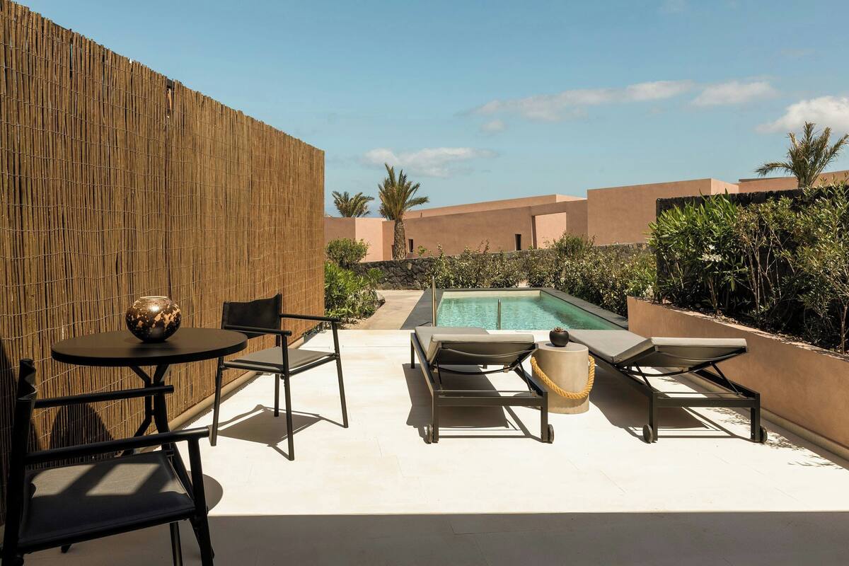 Uma área de piscina no terraço com espreguiçadeiras, uma mesa e um vaso decorativo.