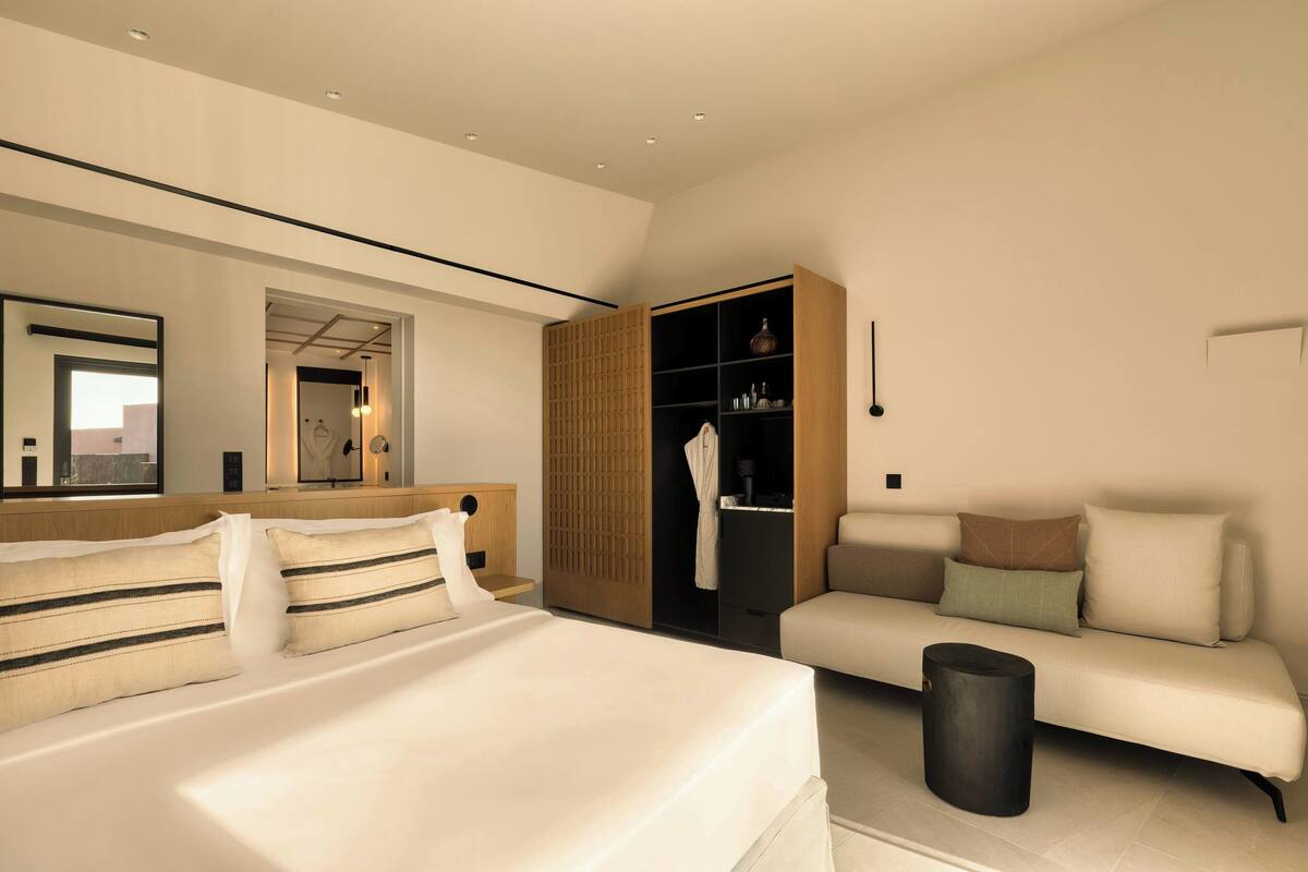 Quarto de hotel moderno com uma cama grande, um sofá, um guarda-roupa e um espelho.