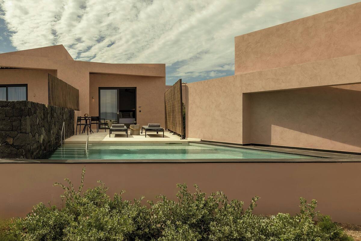 Uma área de piscina moderna com uma parede de pedra, cadeiras de descanso e céu claro.