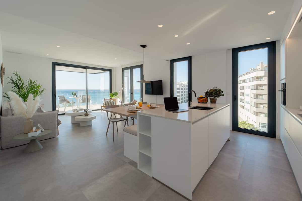 Cozinha moderna com ilha central, área de jantar com cadeiras e amplas janelas com vista para o mar.