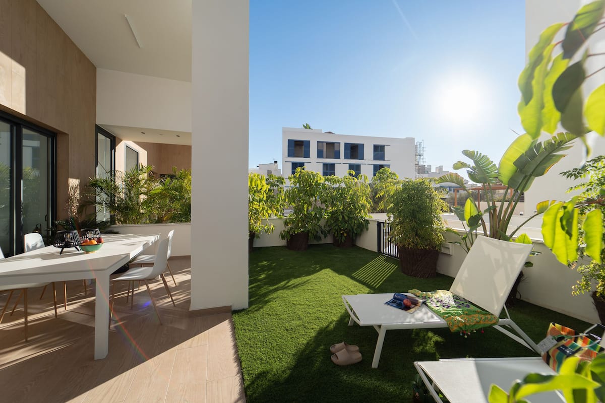 Um pátio moderno ao ar livre com mesa e cadeiras de jantar, rodeado por vegetação exuberante e vista para um horizonte urbano.
