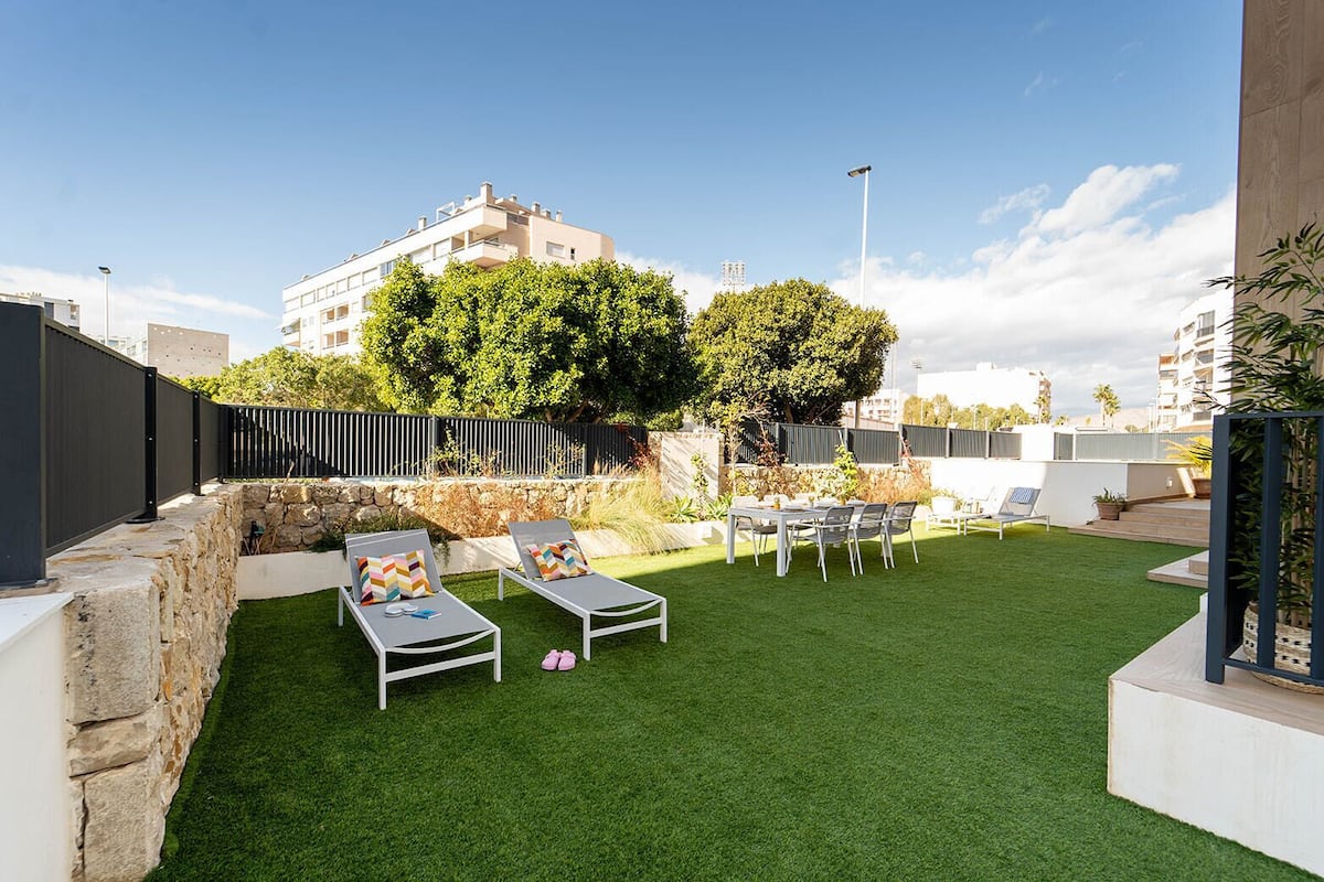 Um jardim no terraço com grama sintética, espreguiçadeiras e uma mesa de jantar.