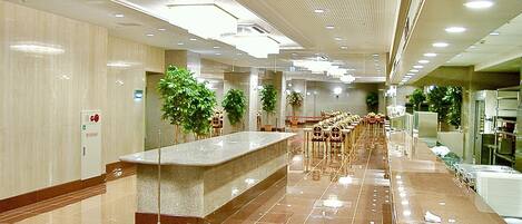 Um hall de hotel espaçoso com um balcão de recepção comprido, várias áreas de estar e diversas plantas em vasos.