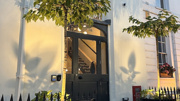 Um edifício com porta preta, escadaria que leva a um andar superior e uma placa indicando 'crescent place' com endereço de site.