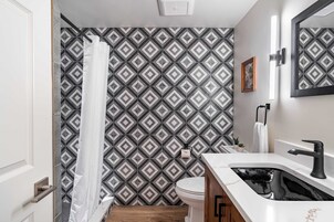 Um banheiro com detalhes em azulejos estampados, vaso sanitário branco, pia preta com espelho e cortina de chuveiro.