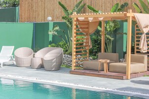 Uma área junto à piscina com cadeiras de vime, uma pérgola de madeira e um sofá.