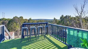 Um deck com guarda-corpo, três bancos e uma sebe verde.