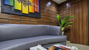Uma sala de estar moderna com um sofá cinzento, uma mesa de centro de mármore e uma parede com pinturas abstratas.
