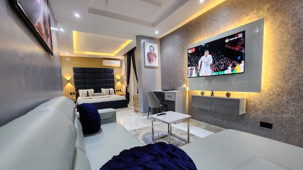 Uma sala de estar moderna com uma televisão de tela plana grande fixada na parede, um sofá, uma mesa de centro e um pequeno espaço para escritório.