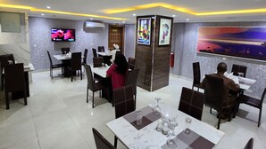 Restaurante com chão de piso de mármore, mesas e cadeiras de madeira, uma TV de tela plana e um grande mural na parede.