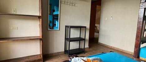Quarto com cama, ventilador de teto, televisão e uma mesinha.